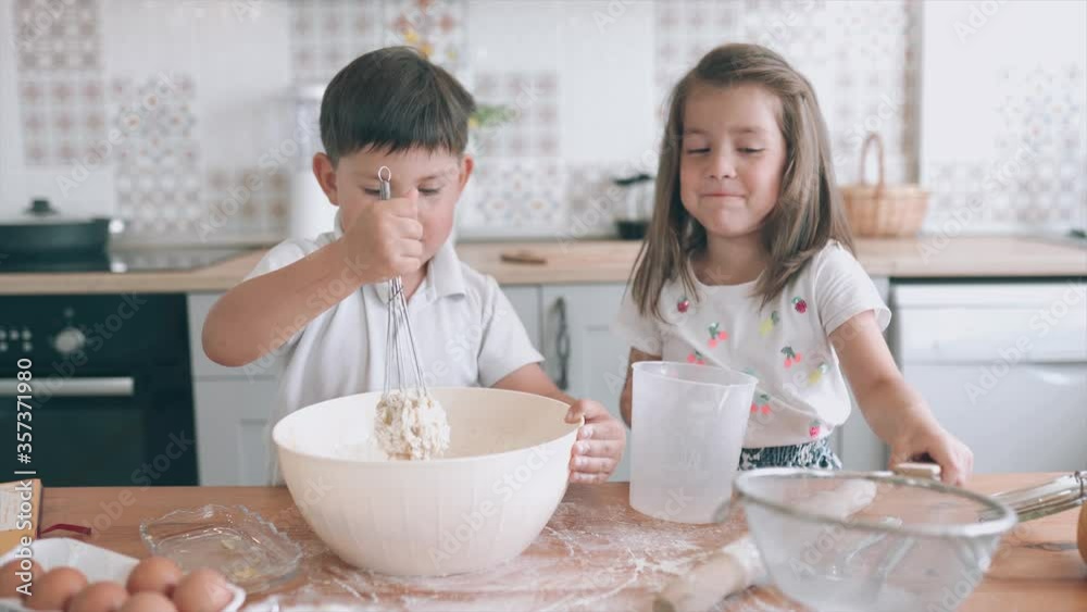 Vidéo Stock Funny kids cooking together. Girl is beating the dough, sift the flour. Brother and ...