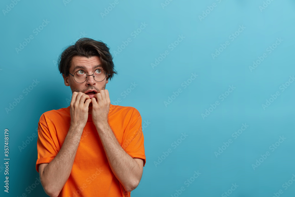 Scared nervous man bites finger nails and looks upwards with anxious ...