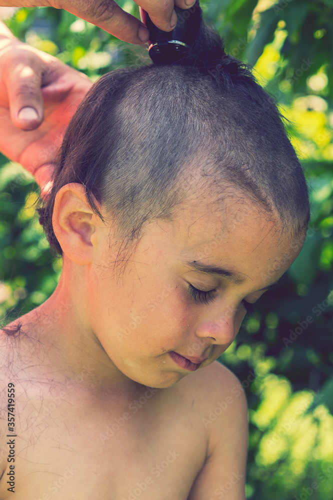 hand holds an electric hair clipper and cuts the boy's long hair ...