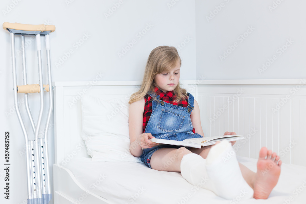 Schoolgirl with a broken leg at home reading a book in bed. Her leg is ...