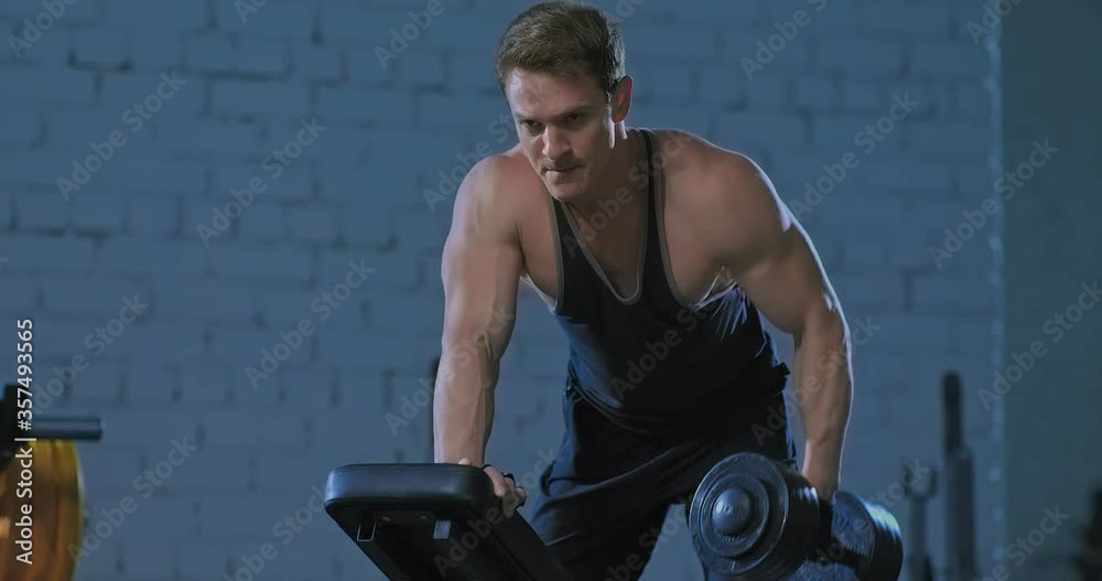Muscular athlete doing dumbbell pull with emphasis on the bench ...