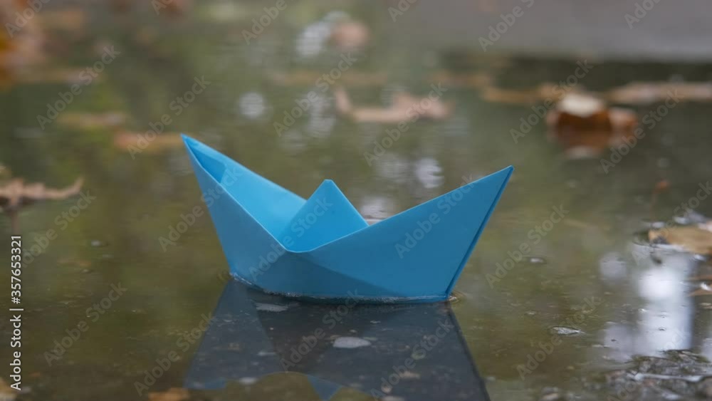 Paper boat in the rain. Blue paper boat in a puddle with autumn leaves ...