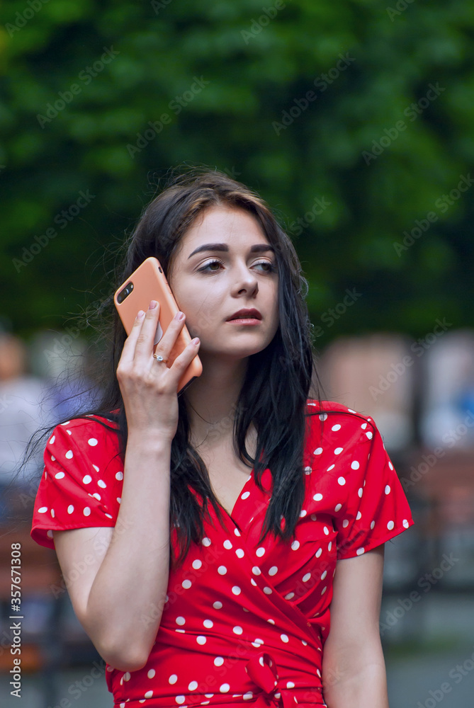 Sad girl walks around the city. A woman in a dress is talking on the ...