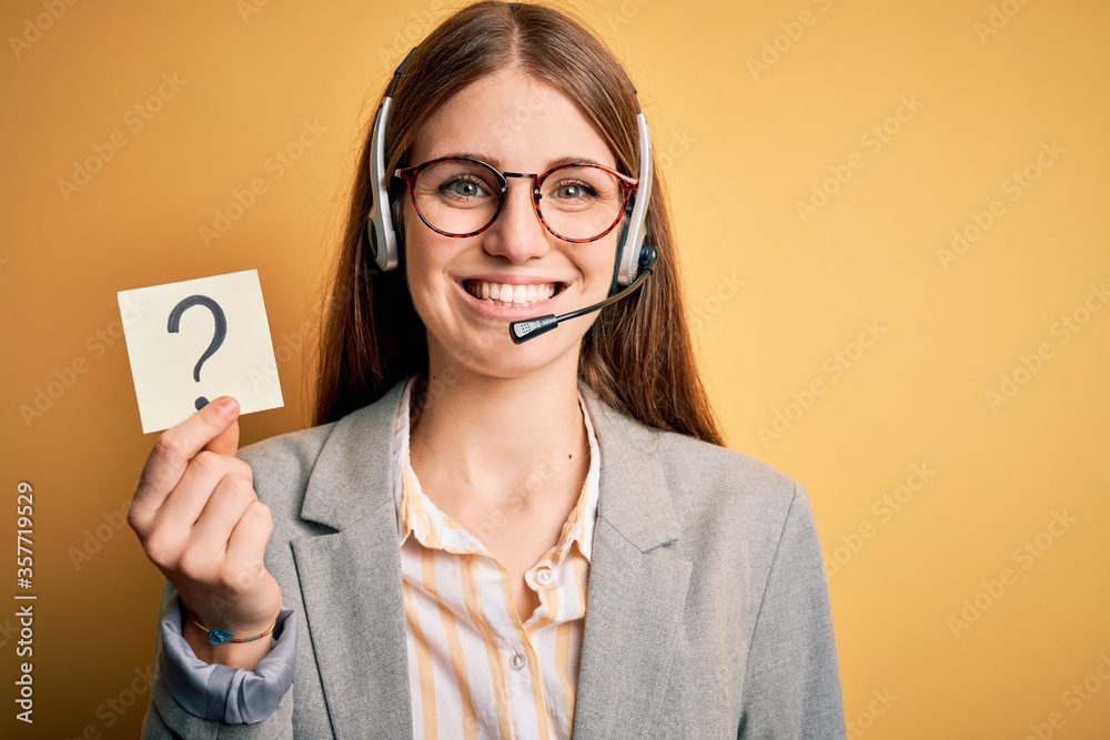 Young redhead call center agent woman using headset holding question ...