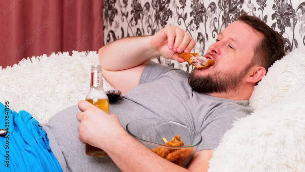 fat man drinks beer and eats unhealthy food chicken wings, bored in ...
