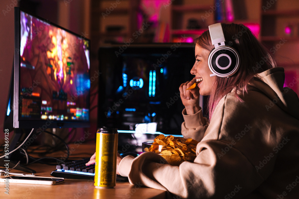 Image of delighted cute girl eating chips while playing video game ...
