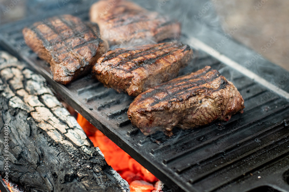 Beef steaks grilling on a cast iron plate on a camp fire. Campfire ...