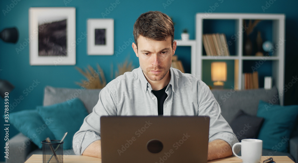 Front view of consumed young man working on laptop computer sitting at ...