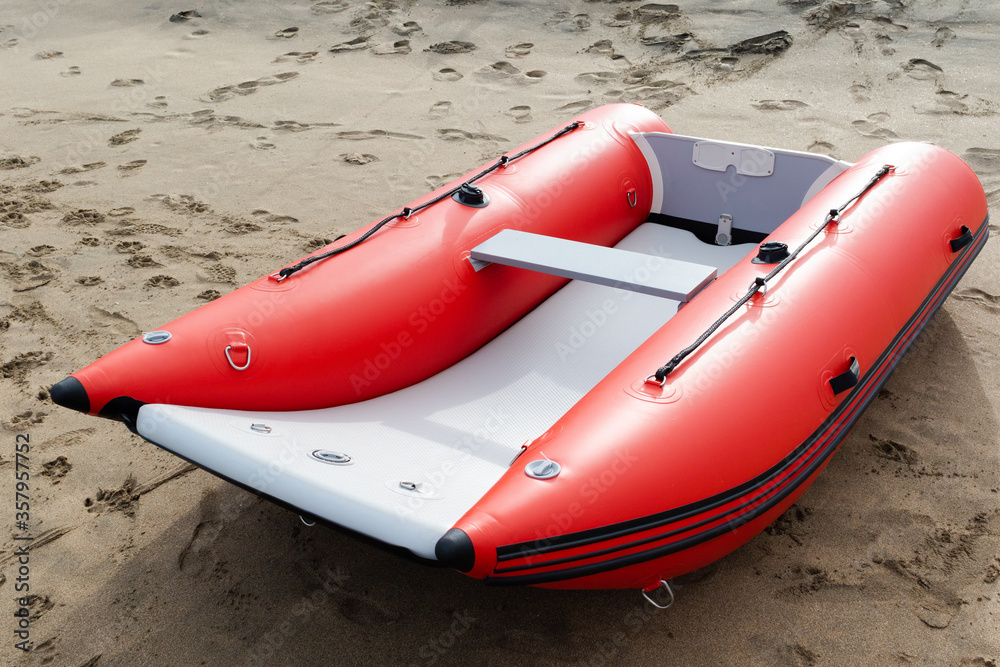 An inflatable boat on the beach it is red in color with a grey floor ...