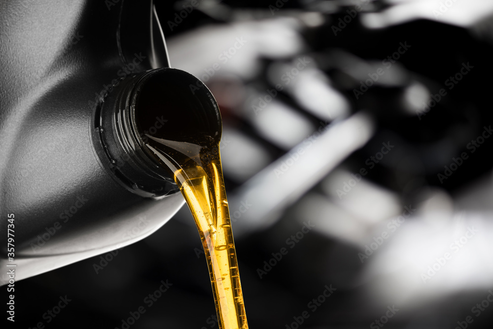 Pouring oil lubricant motor car from black bottle on engine background ...