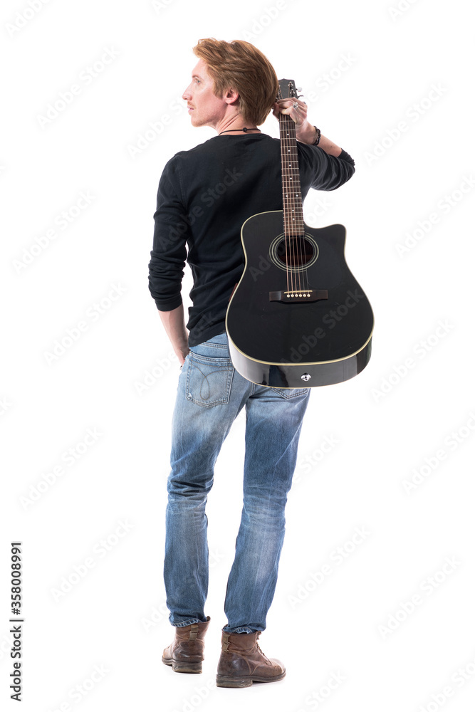 Back view of young rocker musician carrying guitar on shoulder looking ...