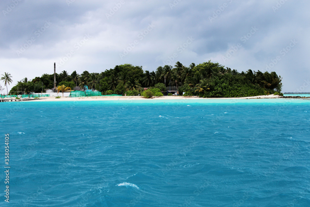 Small traditional village on Maldives island, green palm trees in azure ...