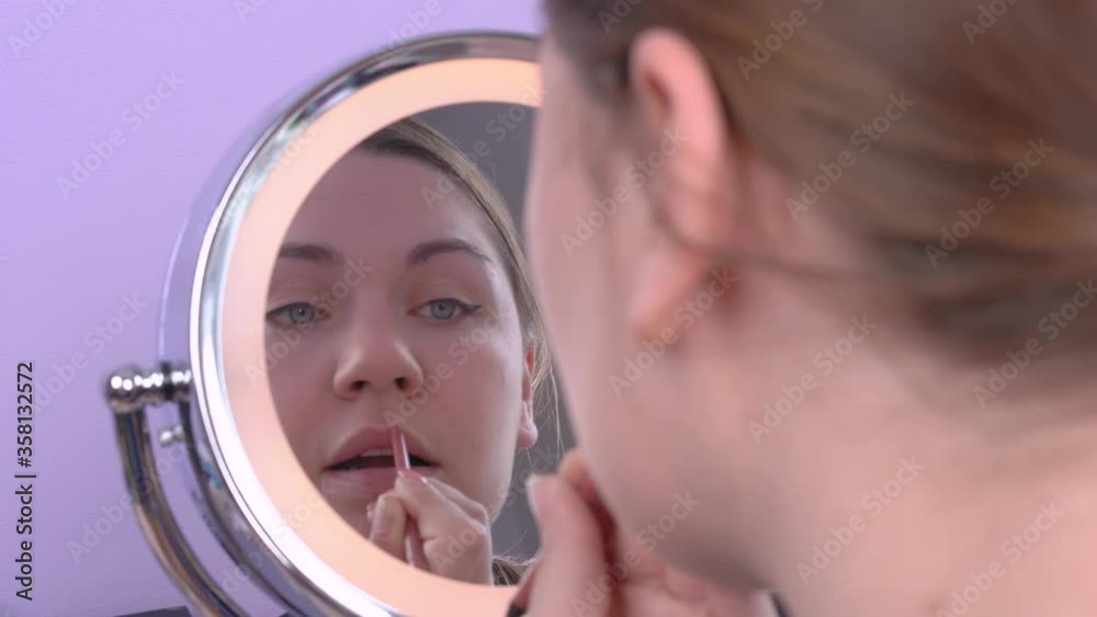 Attractive girl gently puts makeup on her face, paints lips with a ...