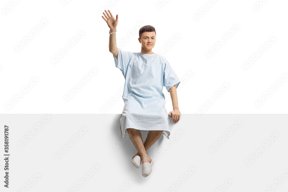 Young male patient in a hospital gown sitting on a panel and waving ...