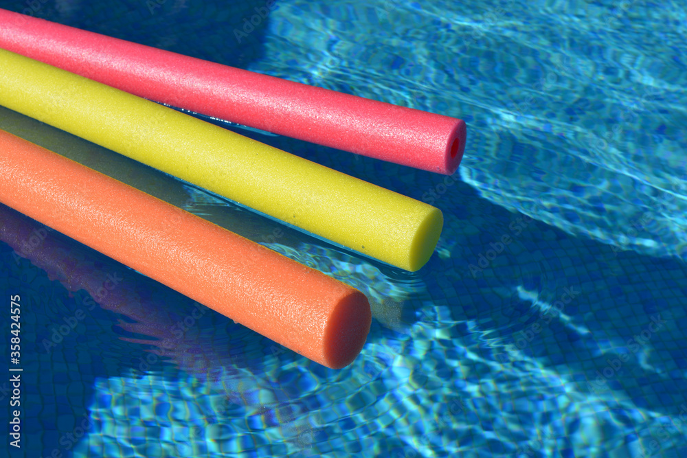 Red, orange and yellow pool noodles floating in a swimming pool ...