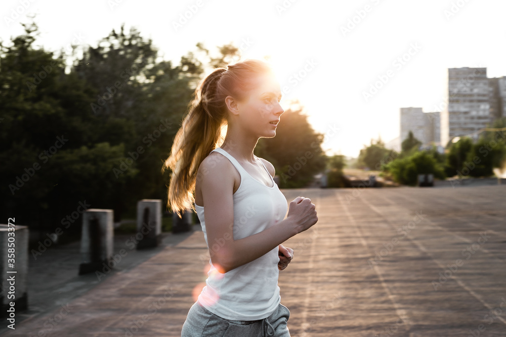 Female runner jogging on the street. The girl with blonde long hair in ...