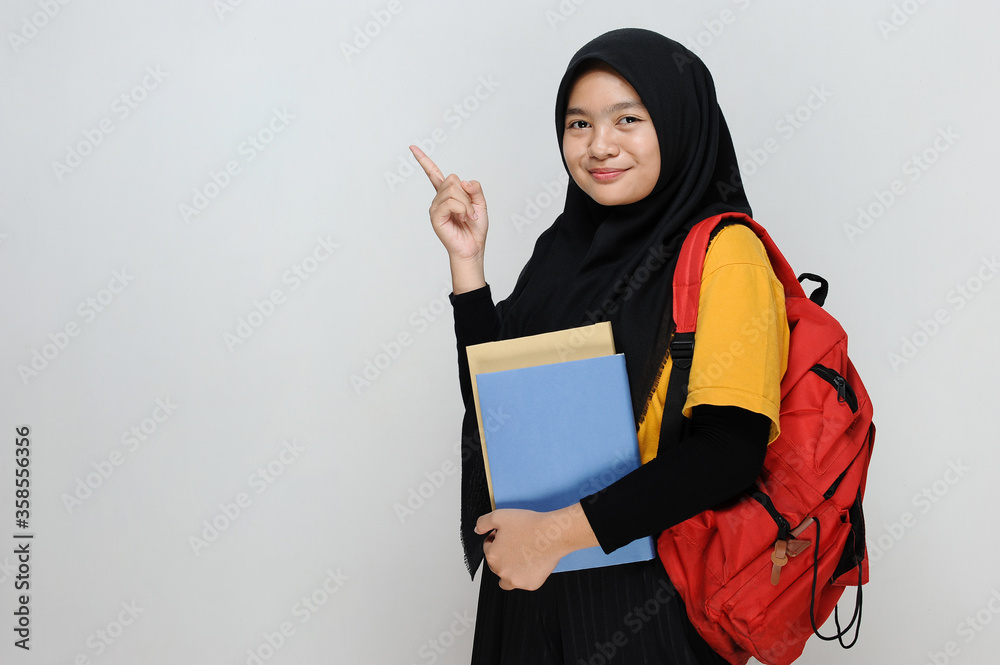 Portrait of teenager muslim female student in hijab pointing at copy ...