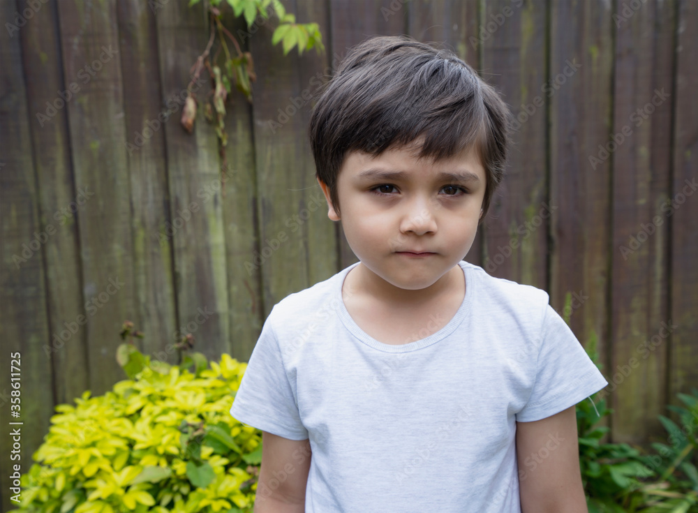 Emotional portrait of lonely child standing alone next to wooden wall ...