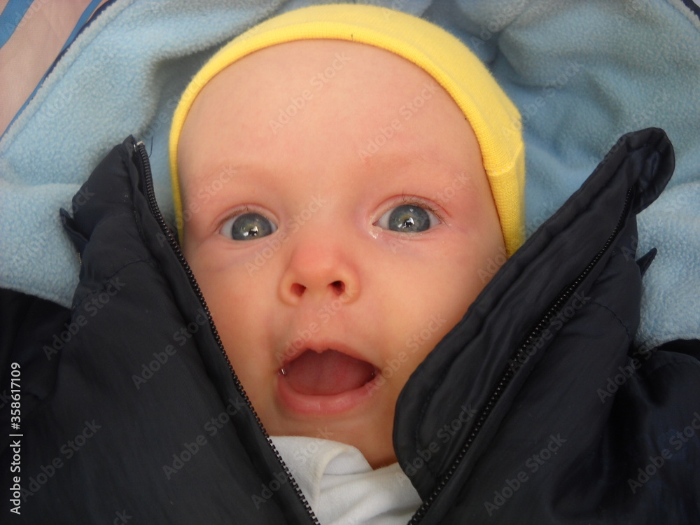 The baby lies in a stroller and opens his mouth in surprise. The child ...