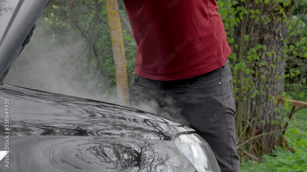 Caucasian male driver raises the hood of car and eliminates the ...