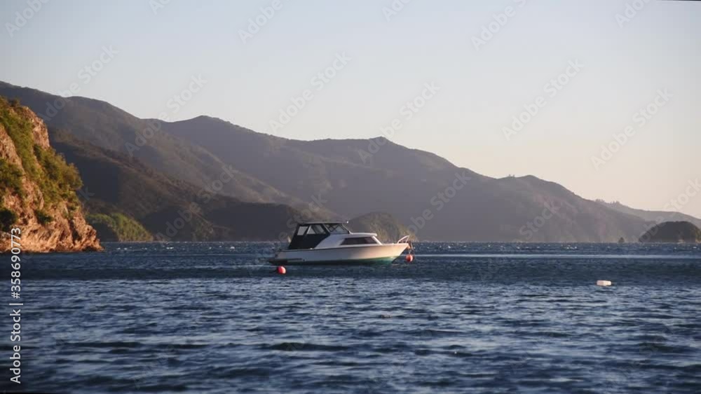 Pan left showing a white motor boat on deep blue water next to a cliff ...