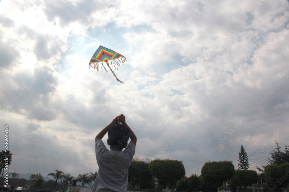 niño latino jugando vuela papalote en cielo con nubes y sol brillante ...
