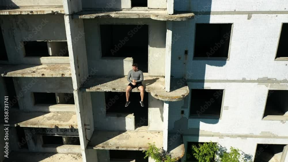 Male athlete showing muscles outside derelict building, Zoom out drone ...