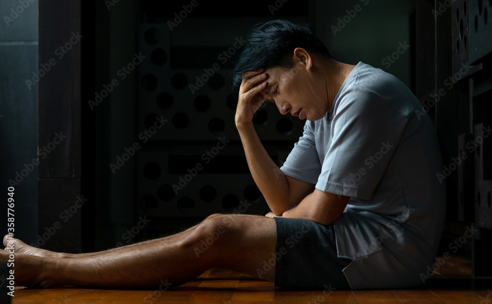 Portrait of unhappy depressed adult Asian man sit on the floor in low light room with holding ...