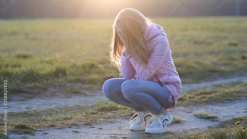 Girl 12 years old crying squatting in the sunset. Stock Photo | Adobe Stock