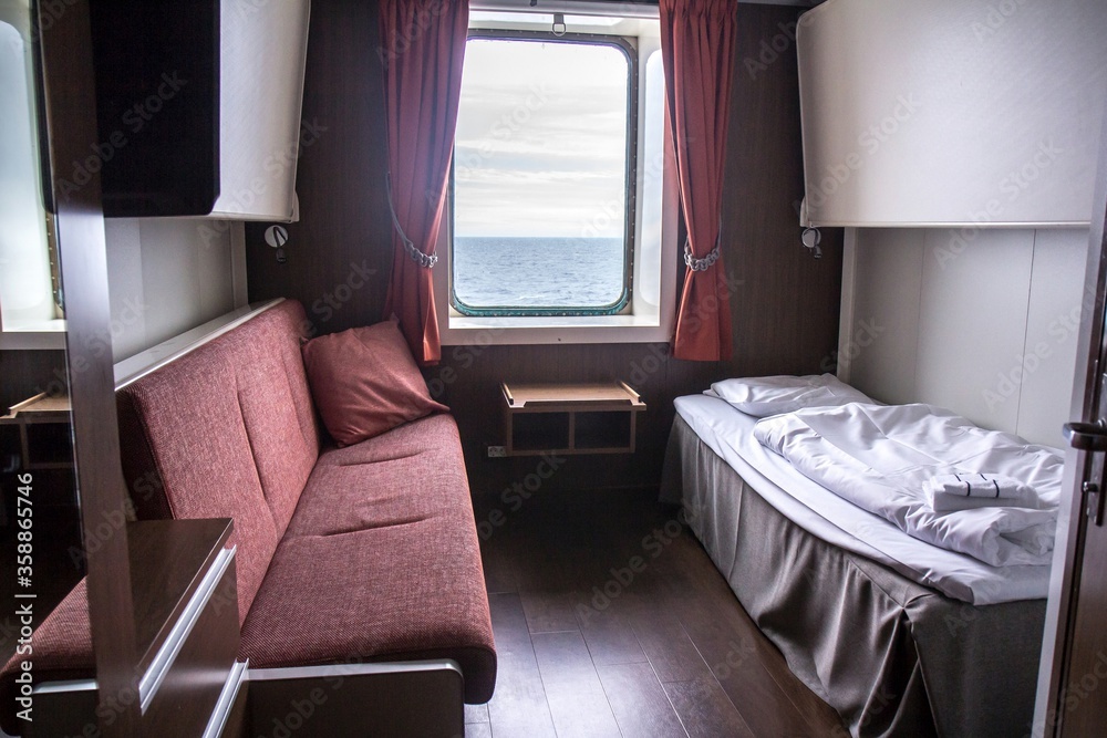 Interior of small but light cabin in passenger ship with window, bed ...