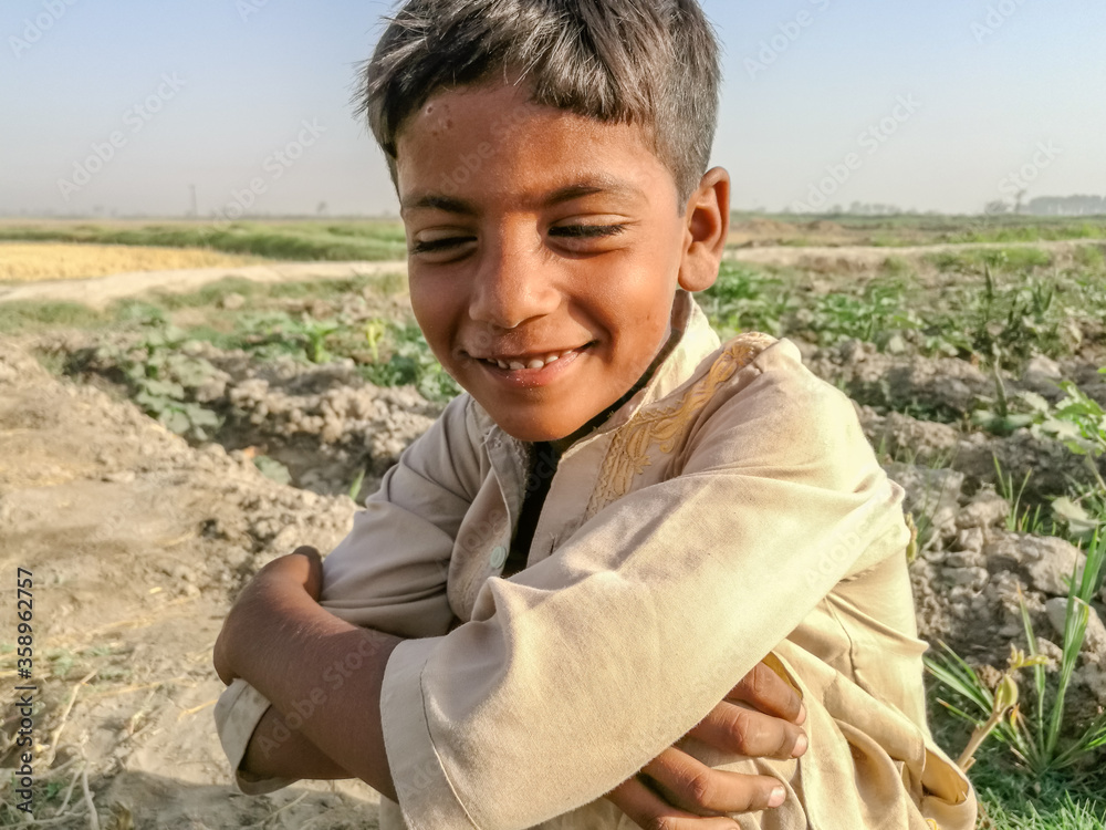 a poor cute smiling boy in a village wearing recycled used clothes ...