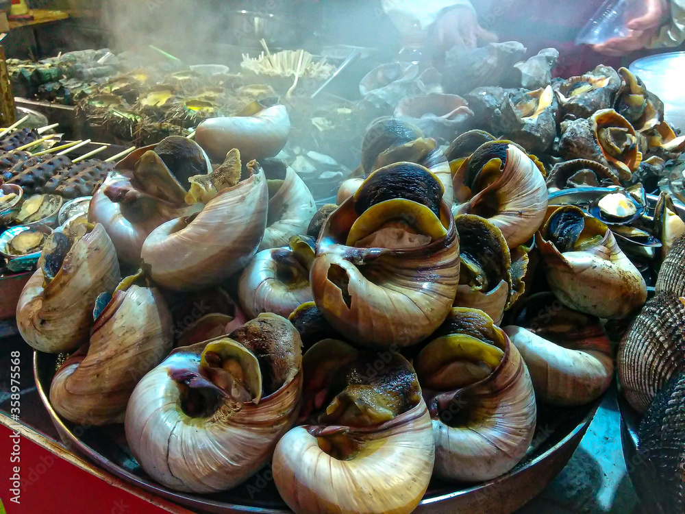 Large snails cooked over an open fire at a street food market in ...
