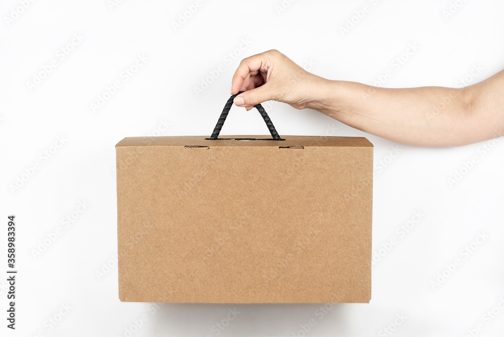 Female hand holds a cardboard box by the handle on a light background ...