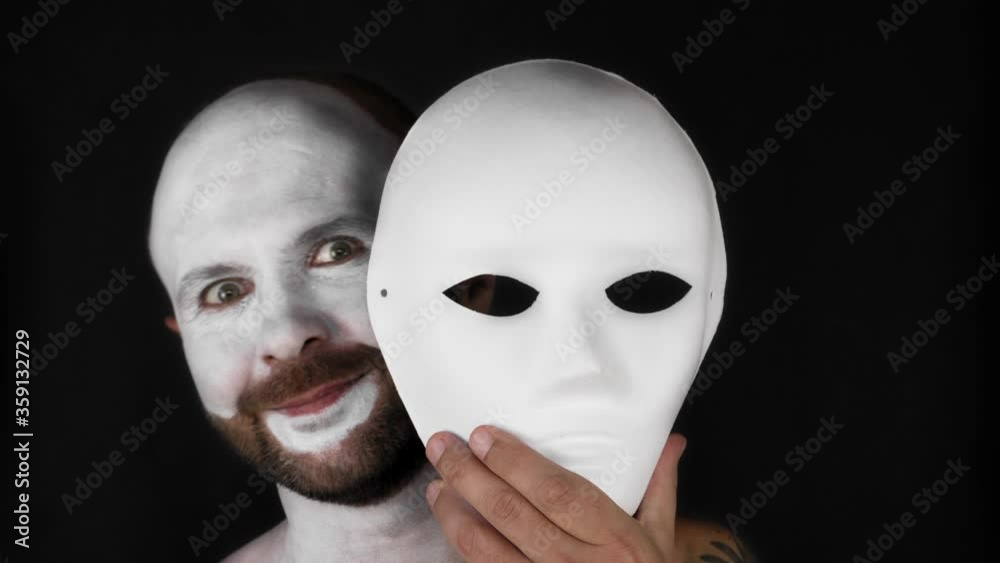 A mime man takes off a white theater mask. Man on a black background ...