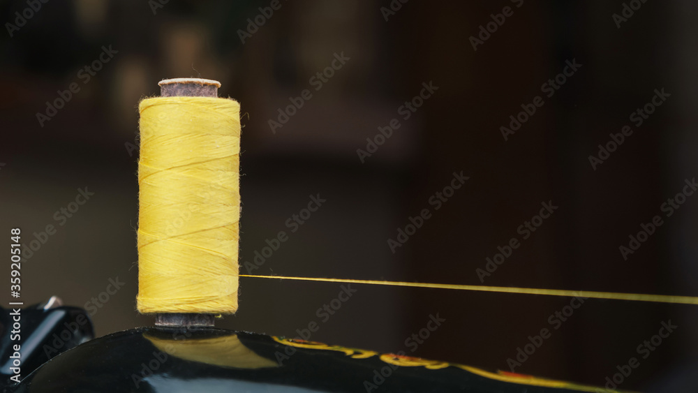 bright yellow thread on spoon pin of old black sewing machine in light ...