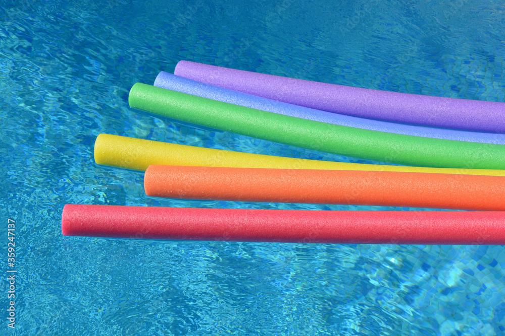 Rainbow coloured pool noodles floating in a swimming pool on a bright ...