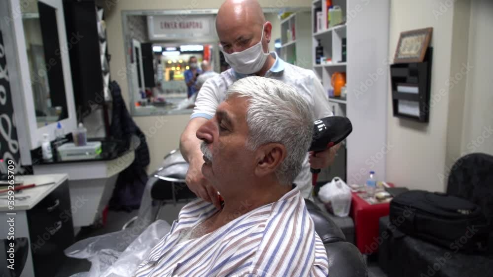 Professional barber in a medical gauze mask on his face making a ...