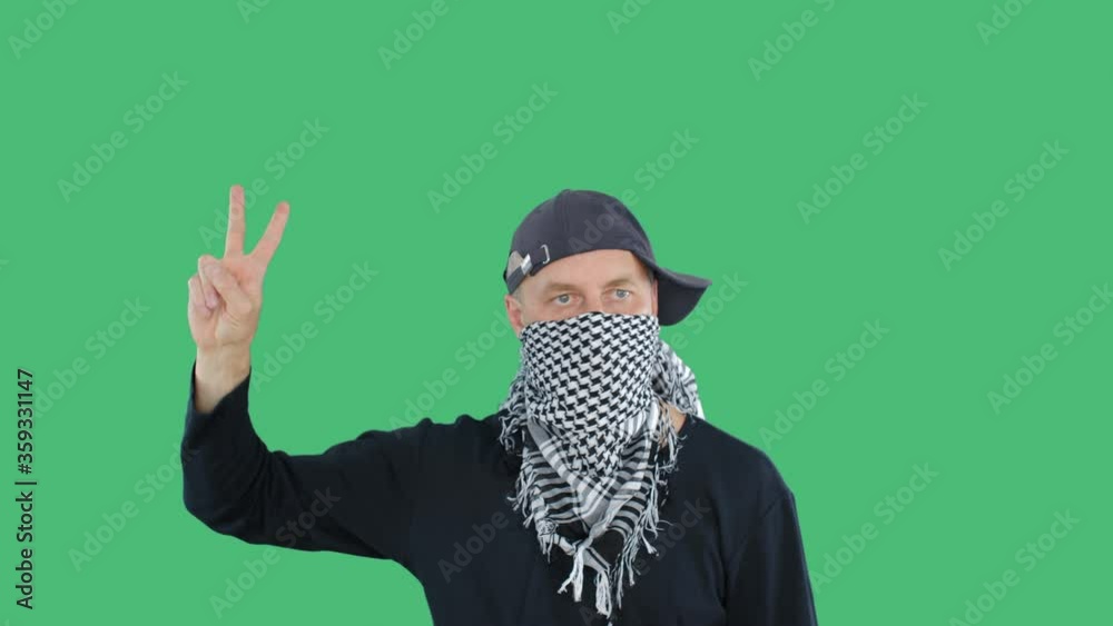 Protester hiding face and showing victory sign during riot chroma key ...