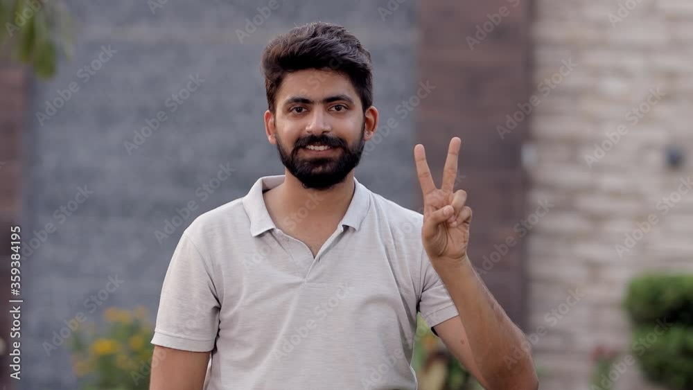 Handsome Indian guy showing a peace sign with a wide toothy smile on ...