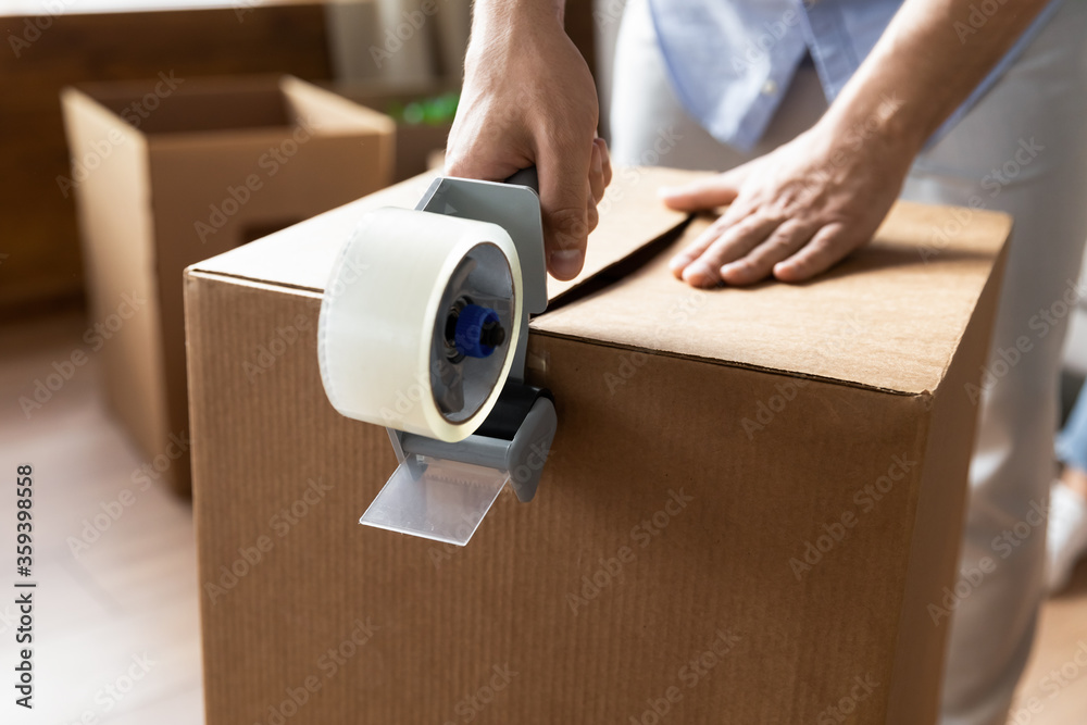 Close up man sealing cardboard box with adhesive tape, using dispenser ...