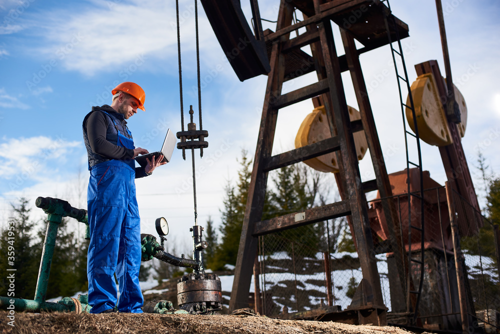 Oil engineer, wearing blue overalls and orange helmet, with a laptop ...