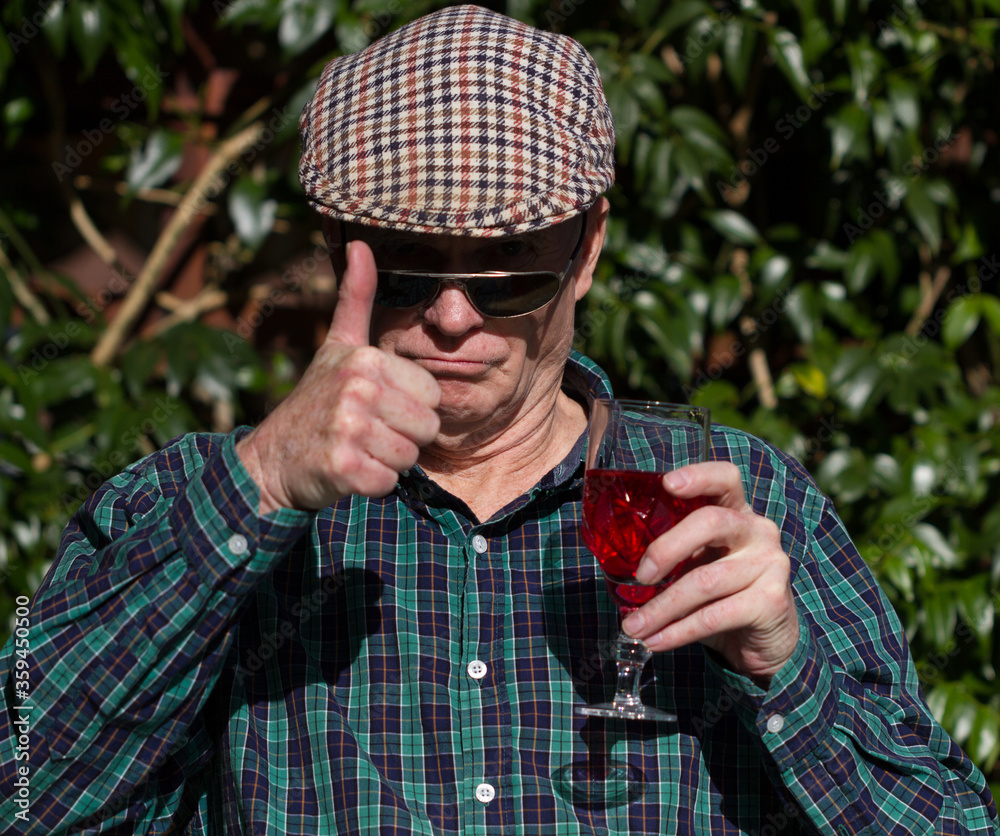 Older man in tweed flat cap drinking red wine and wearing sunglasses ...