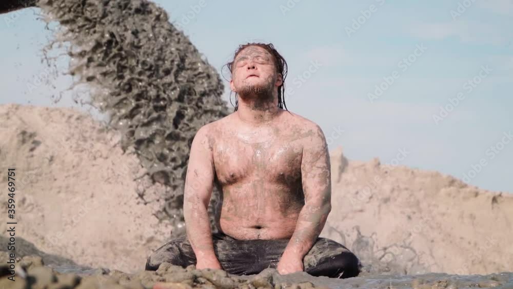 Funny Fat Man with Long Hair Sits in the Mud. Against the background ...