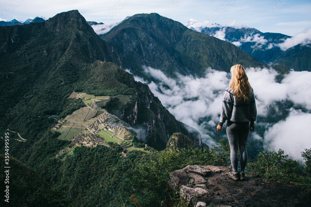 Back view of young woman tourist standing on high peak of mountain and ...