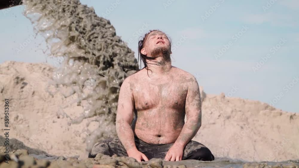 Funny Fat Man with Long Hair Sits in the Mud. Against the background ...