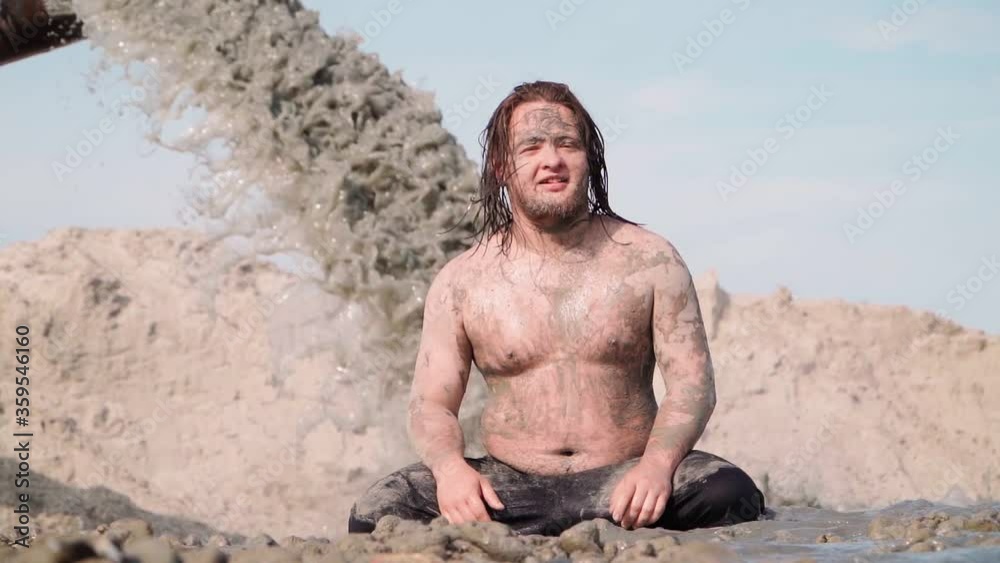 Funny Fat Man with Long Hair Sits in the Mud. Against the background ...