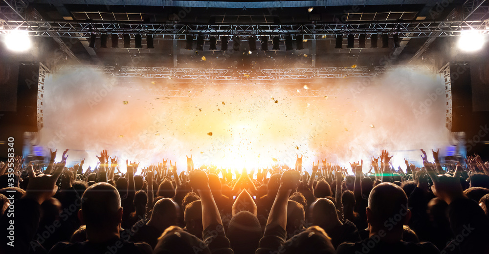 Concert crowd in front of a brightly lit stage; in the background ...