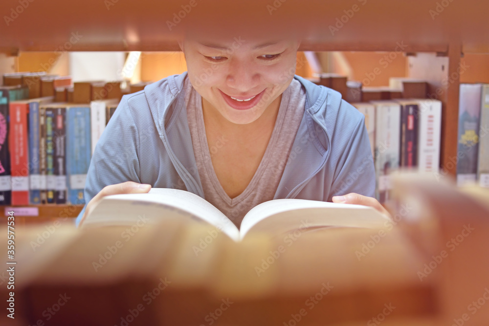 Young Asian woman university student reading book sitting by bookshelf ...
