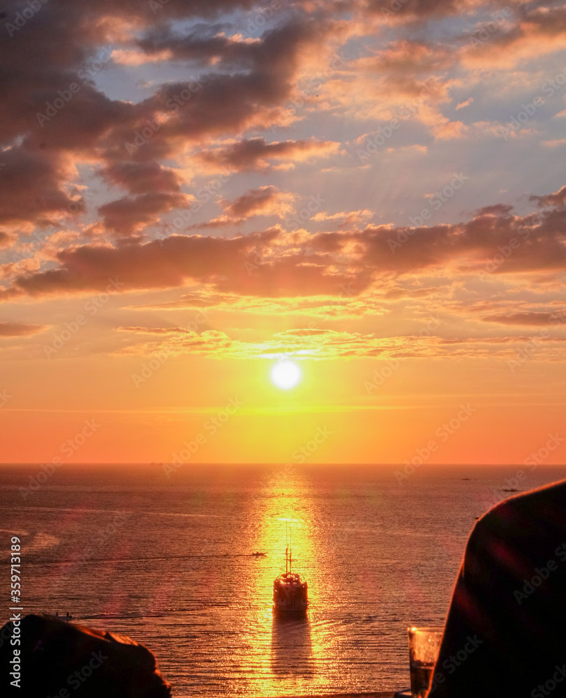 A sailing boat towards the sun, aligned with the sun reflection on ...
