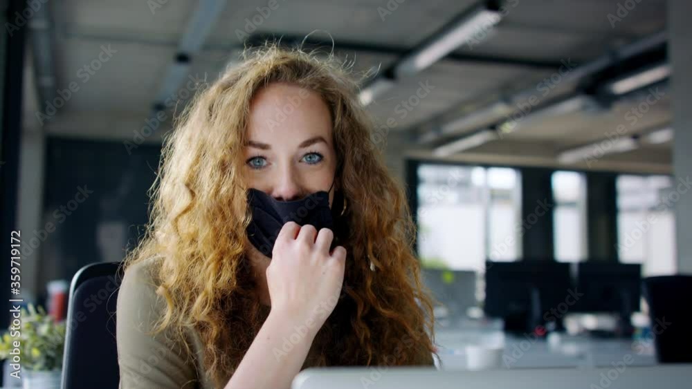 Young woman taking off face mask in office after lockdown, looking at ...
